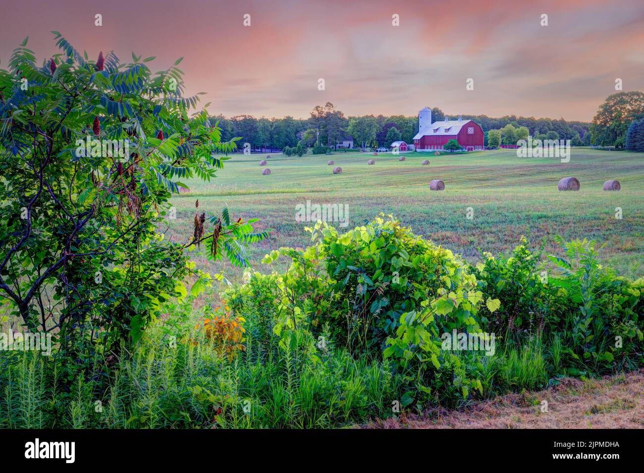 This scene of a barn with round hay bails at sunrise is a typical late ...