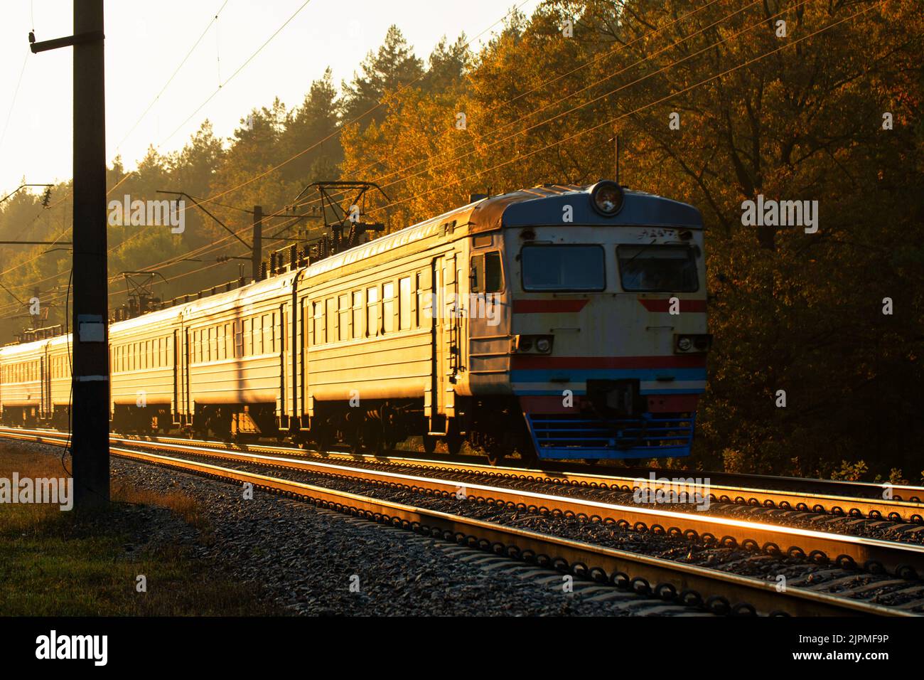 An old passenger train moves through the forest at dawn. Travel by railway. Autumn industrial ...