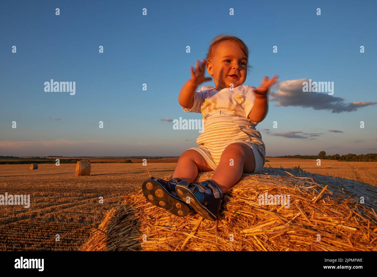 cheerful little boy is sitting on a large round bale of straw. Rest in ...