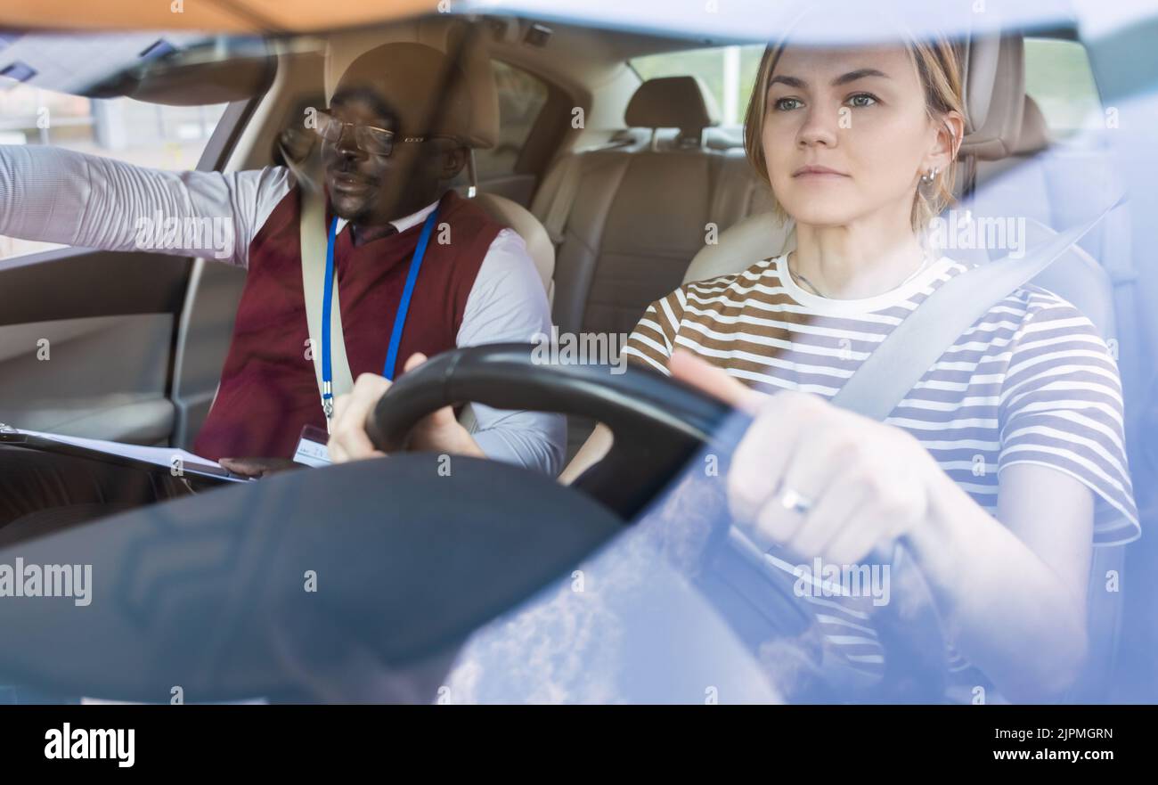 Driving school concept. A car instructor teaches a young woman how to ...