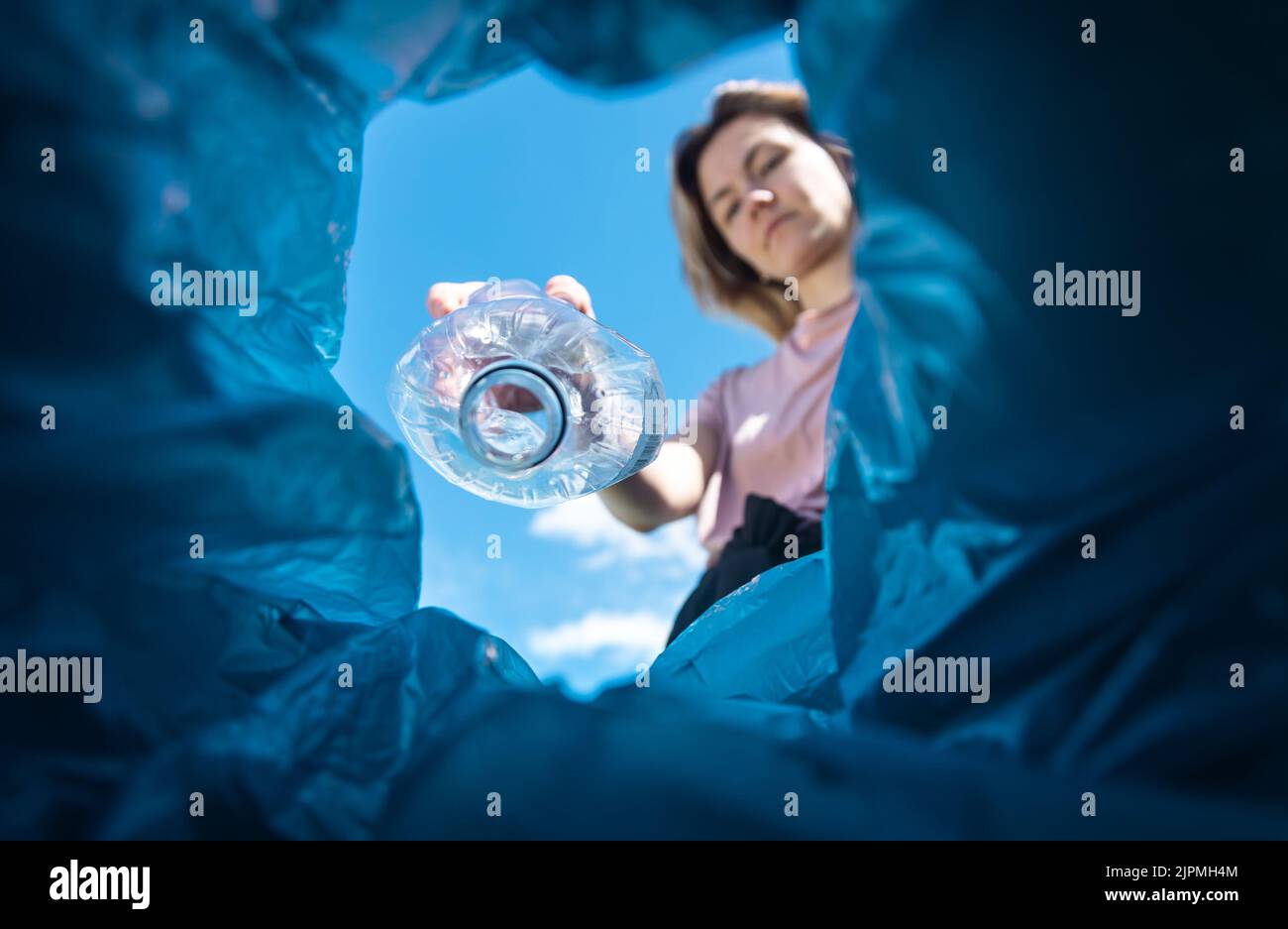 A woman throws a plastic bottle into the trash. Close-up from inside ...