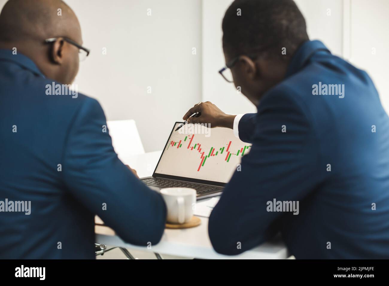 Two African American business partners are working on a laptop studying ...