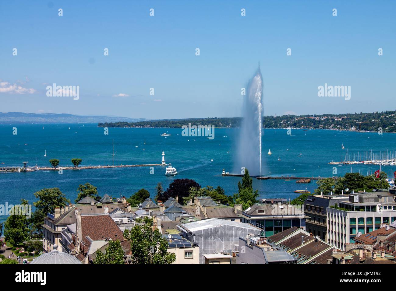 The view of the lake with a fountain and historical buildings of Geneva ...