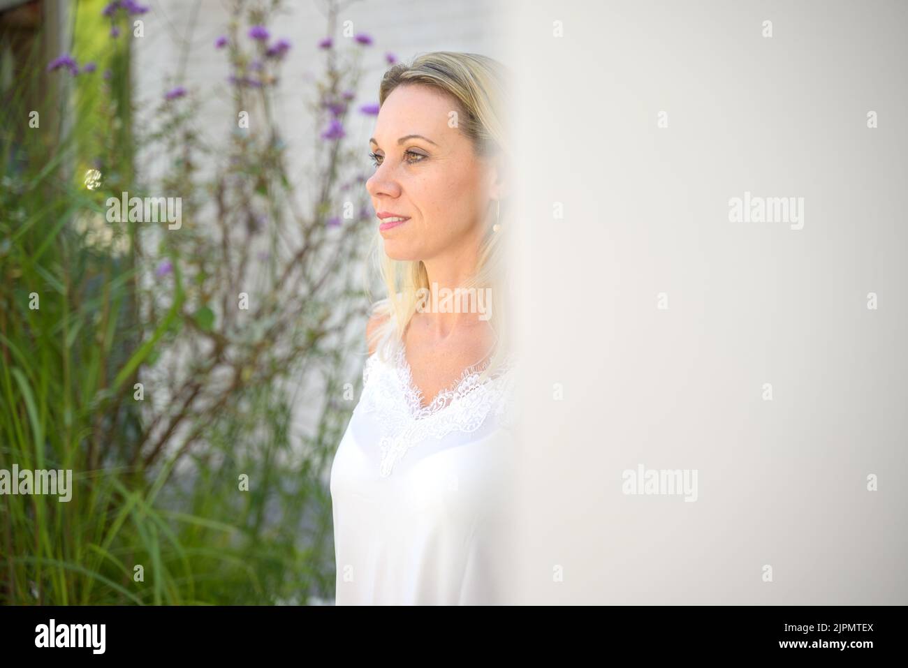 Side view of an elegant blond woman peering around a wall at the camera ...