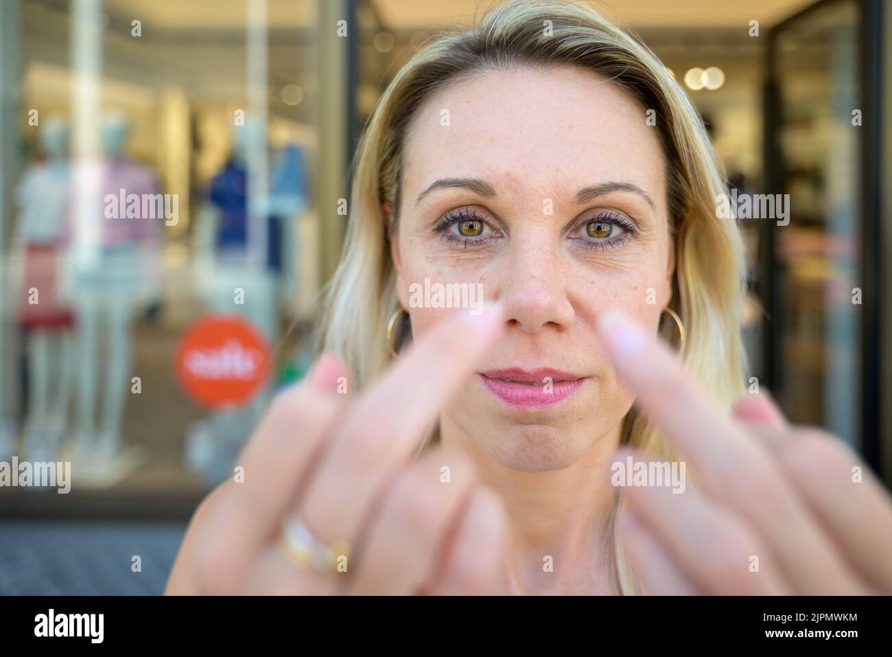 Middle aged blond woman posing in front of urban shops raising her ...