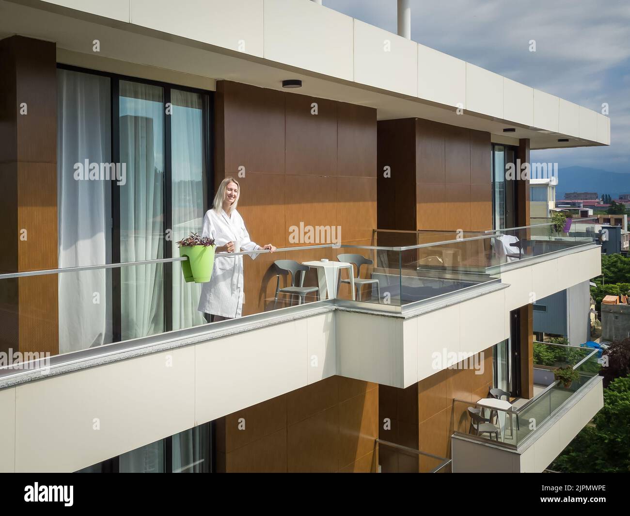 Drone view of a contented blonde young woman in a white coat with a cup ...