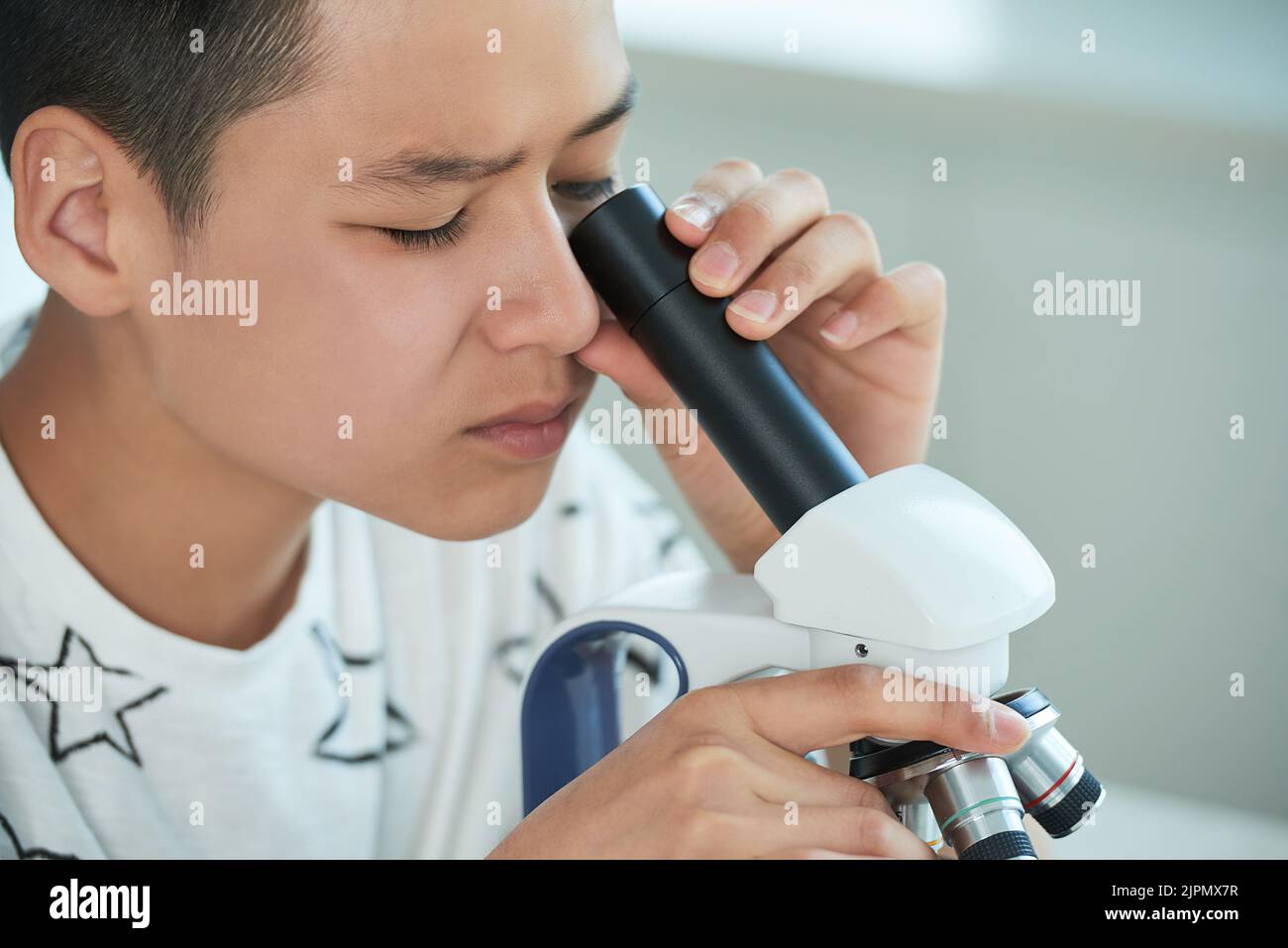 Close-up shot of curious teenage boy studying chemical substance in microscope while having ...