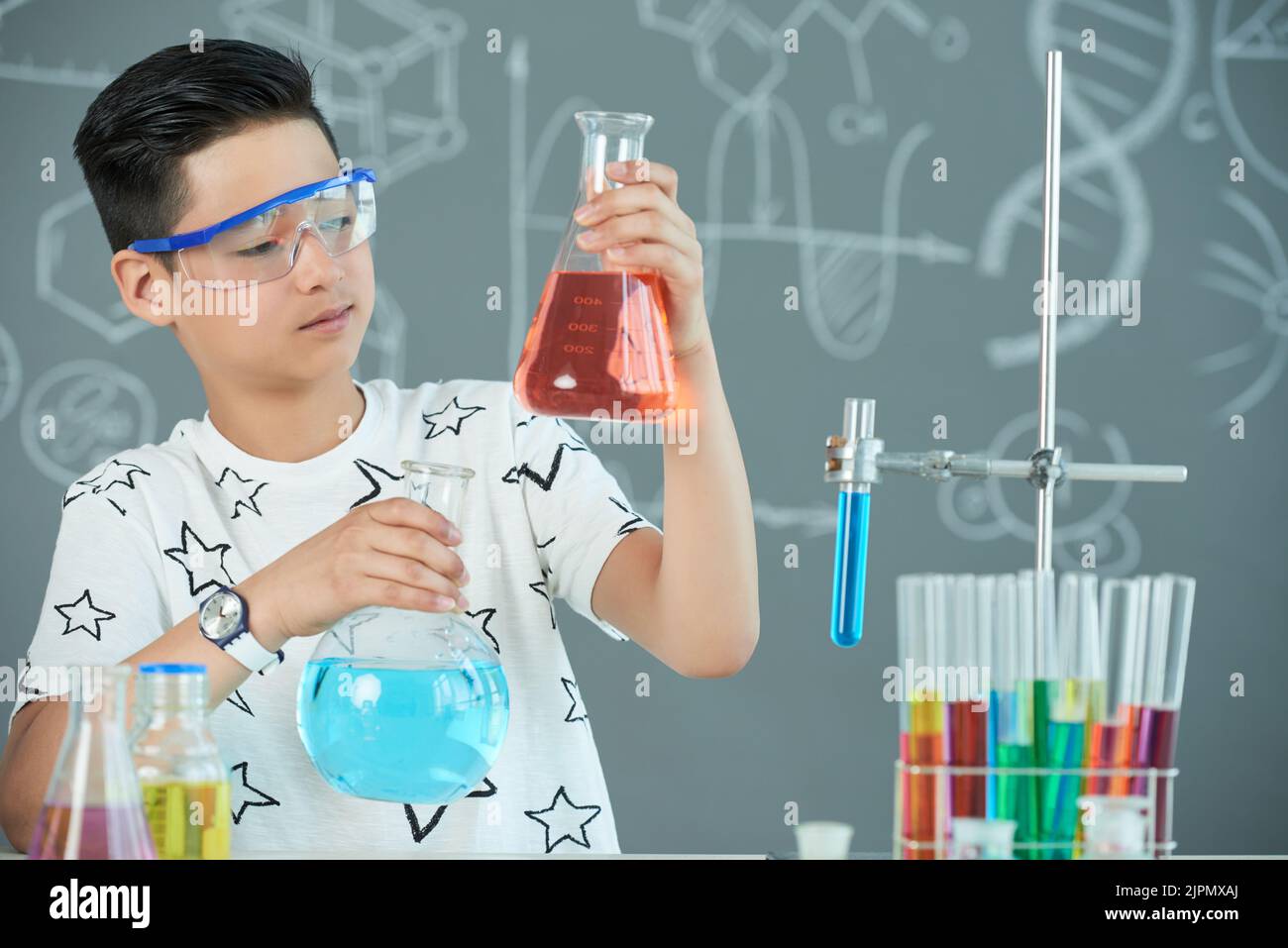 Concentrated Asian student wearing protective goggles holding flasks ...