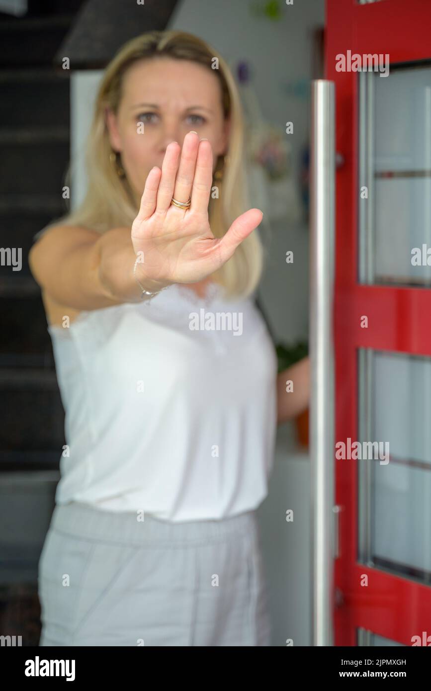 Stern middle aged blond woman holding up her hand in a halt or stop ...