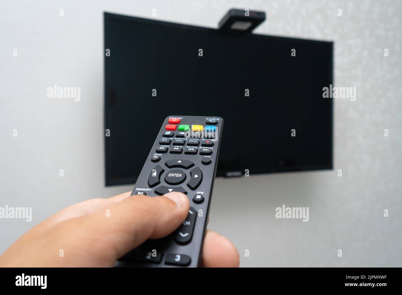 Close-up of a remote control in the hand of a man directing at a black ...