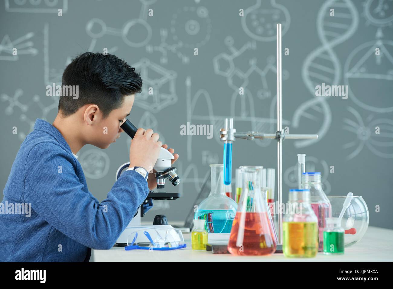 Talented young researcher sitting at school desk and examining sample ...