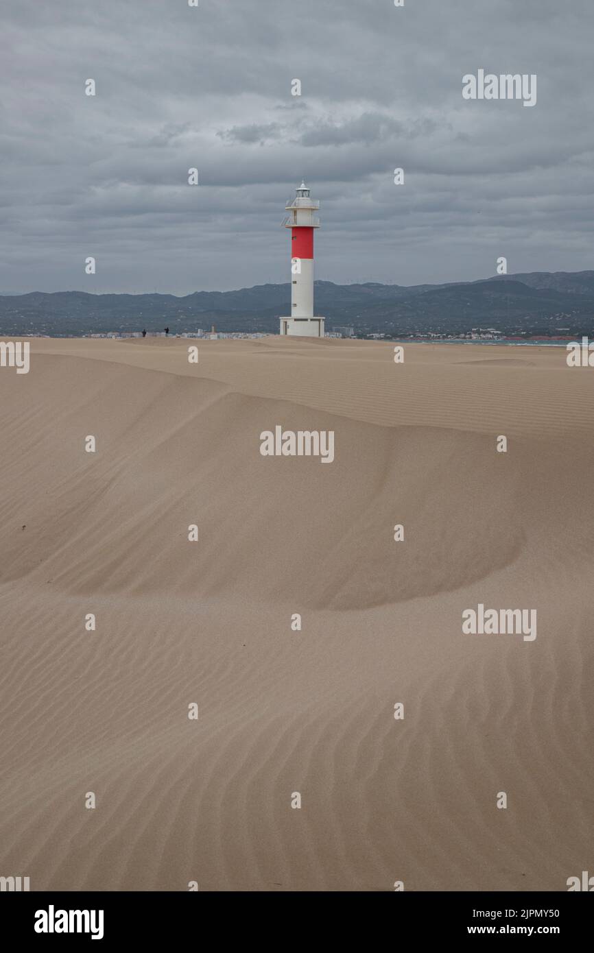 The vertical view of a lighthouse on the sand dune under the cloudy sky ...