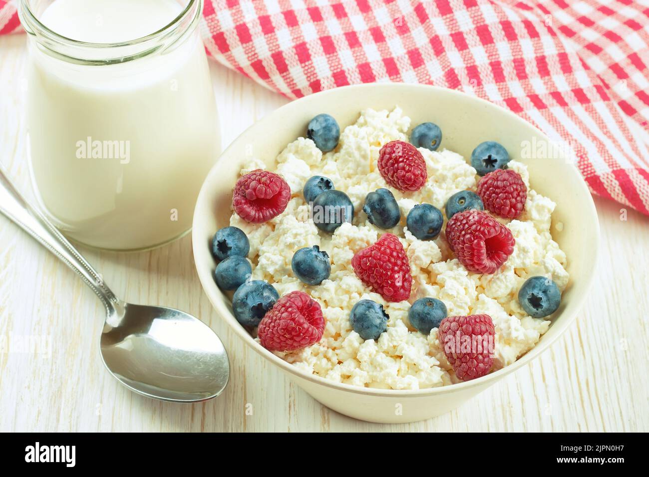 cottage cheese with berries in a bowl and jar of milk on white wooden ...