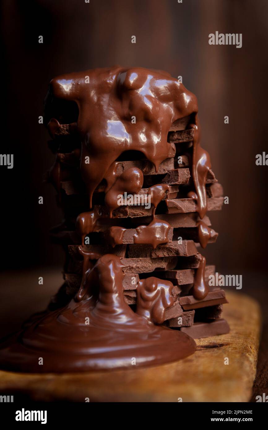 Melted hot chocolate dripping over a pile of chocolate bars on a rustic ...