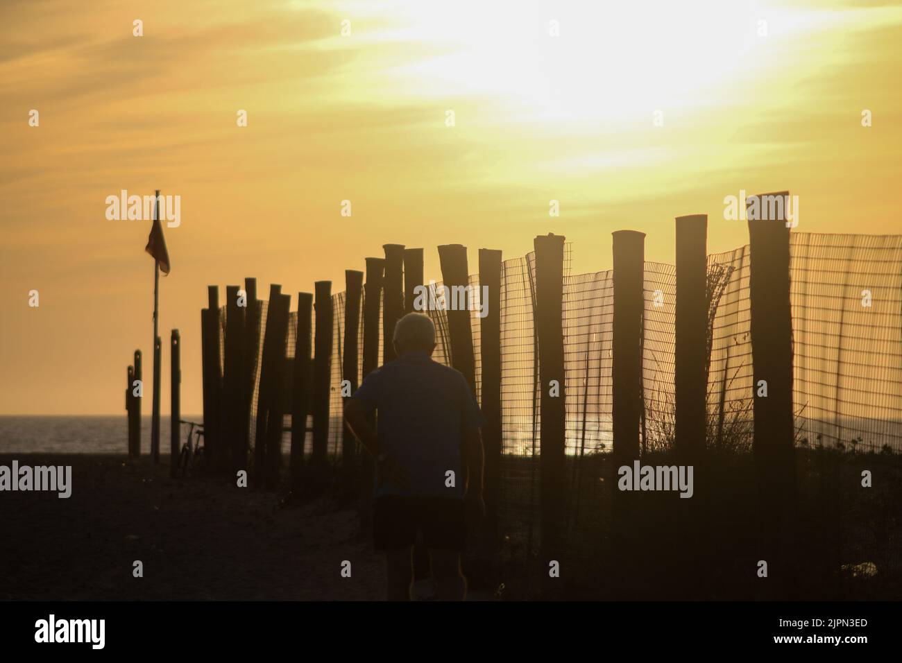 A back view of senior man standing on the beach near the fence during ...