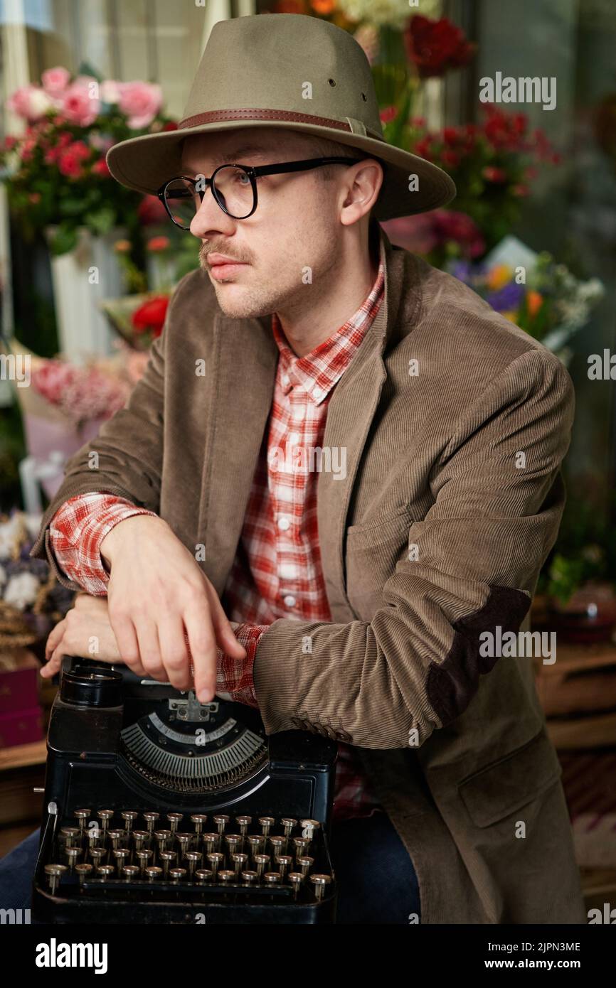 Cute male person in eyeglasses and hat sitting with old typewriter in ...