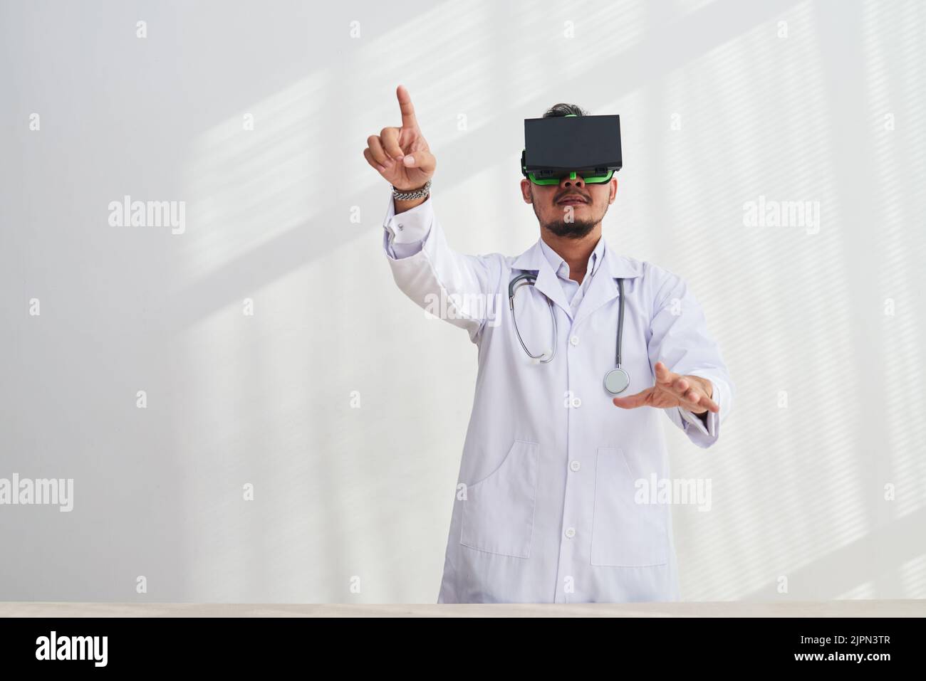 Concentrated bearded doctor wearing white coat pointing at something ...