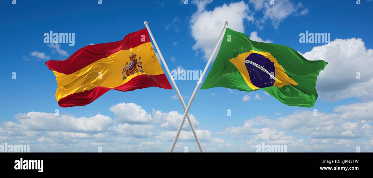 two crossed flags Brazil and spain waving in wind at cloudy sky ...