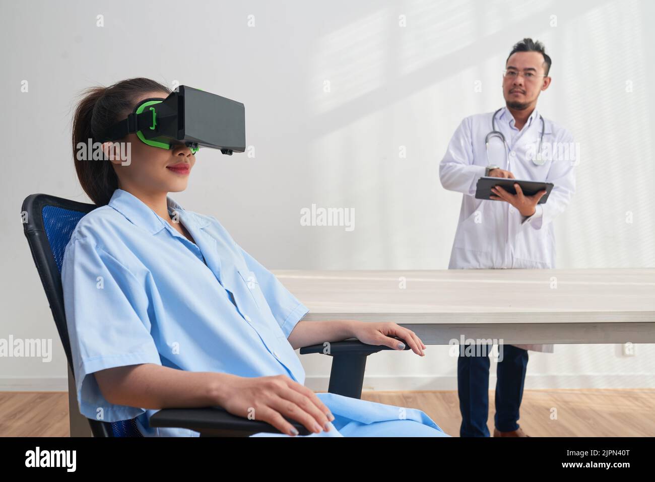 Smiling young nurse sitting on cozy chair and using VR headset while ...