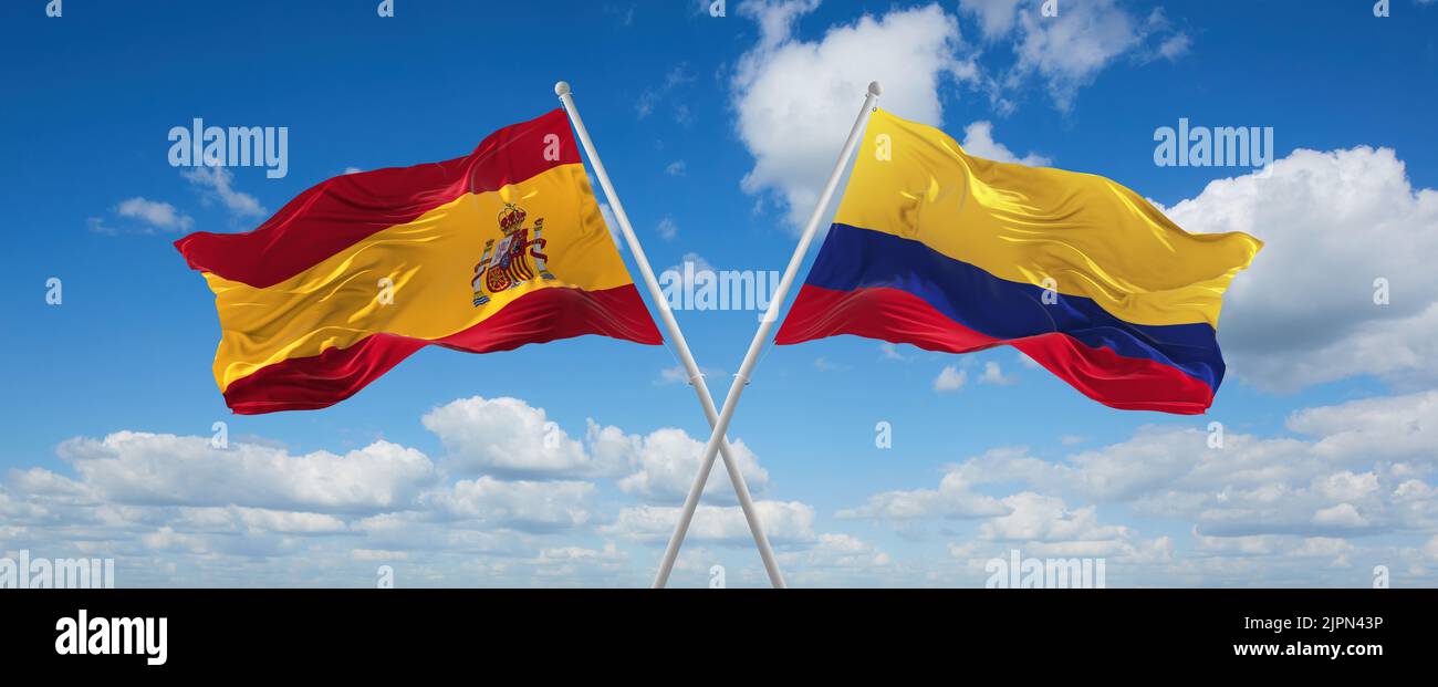 two crossed flags Colombia and spain waving in wind at cloudy sky ...