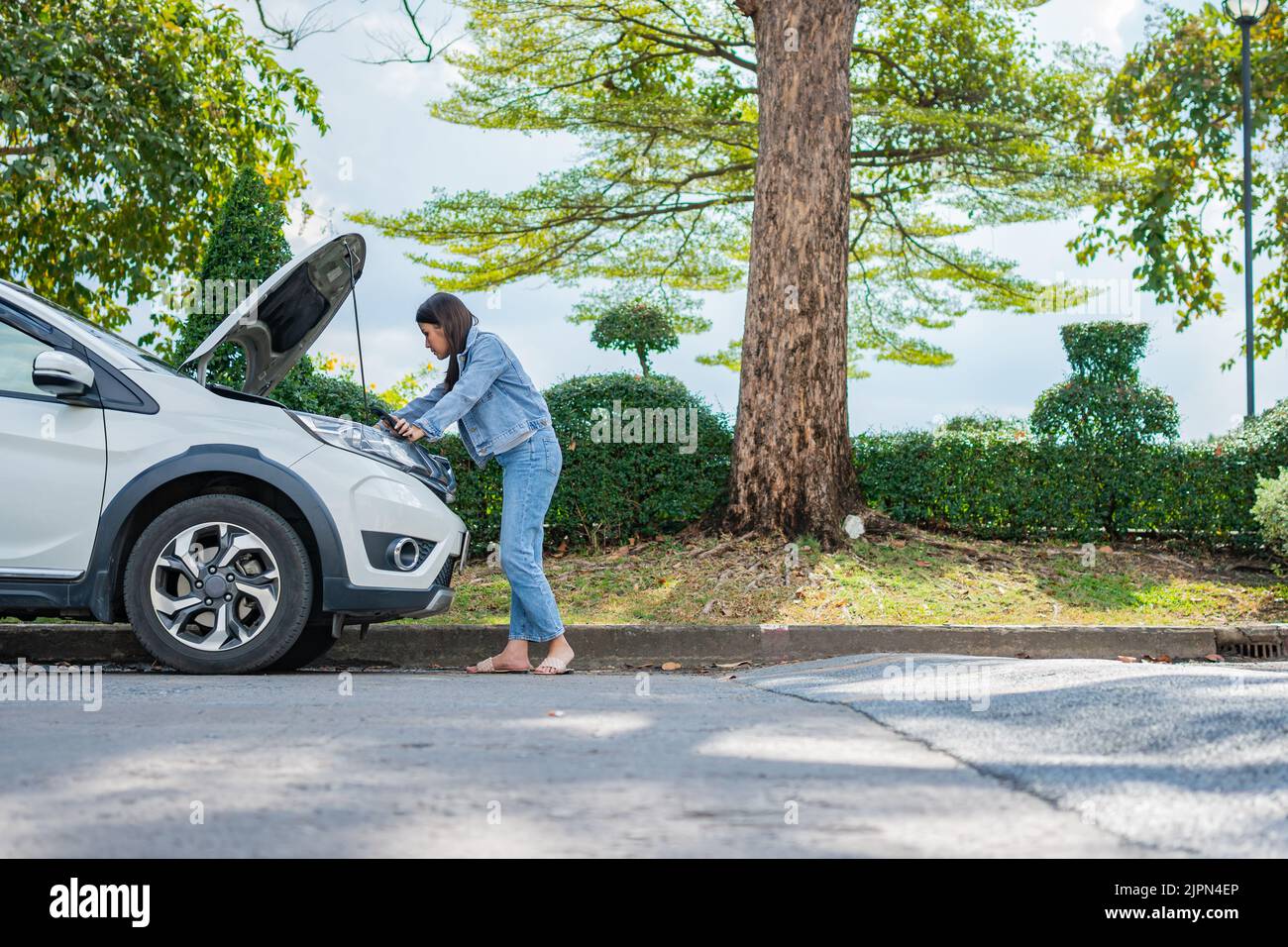 Angry Asian woman and using mobile phone calling for assistance after a car breakdown on street ...