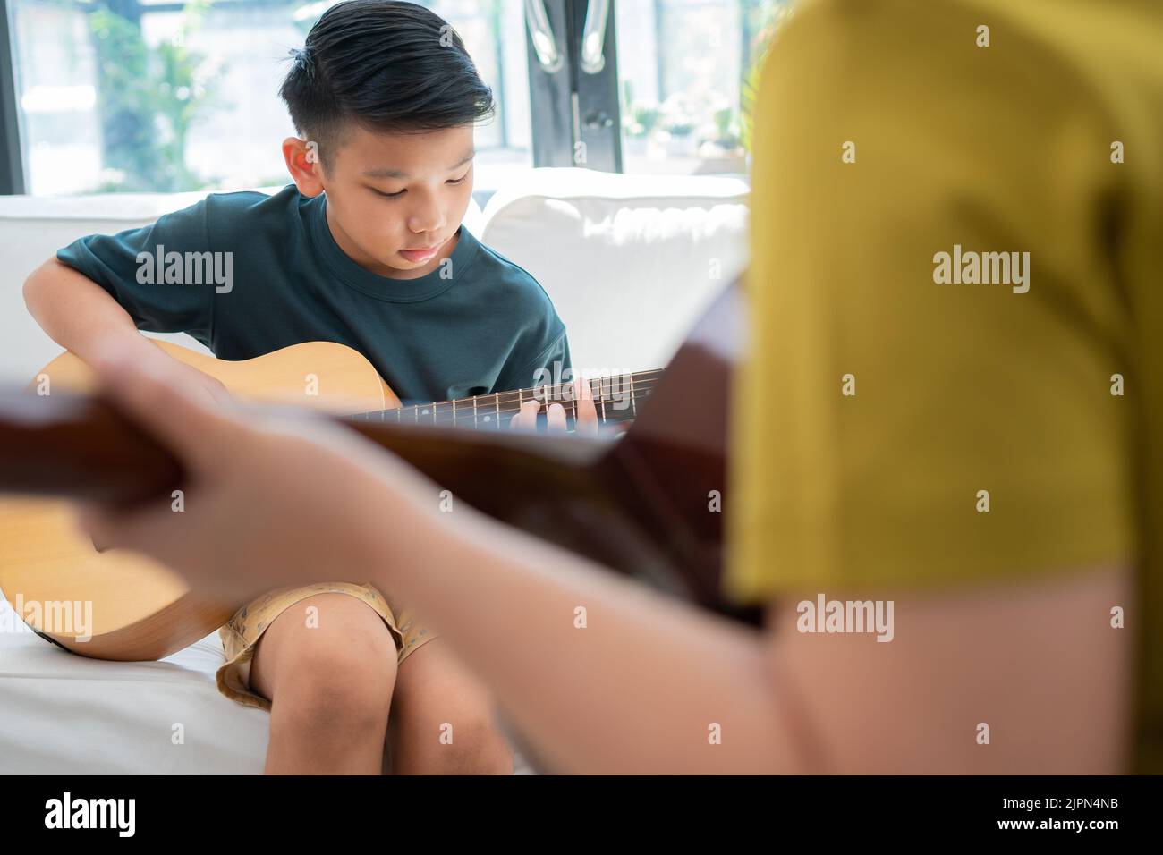 Asian boy playing guitar with father in the living room for teaching ...