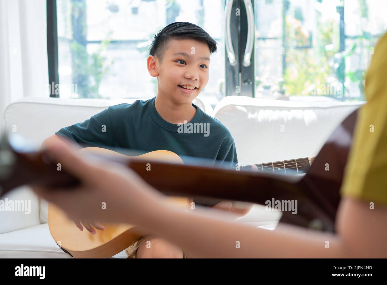 Asian boy playing guitar with father in the living room for teaching ...