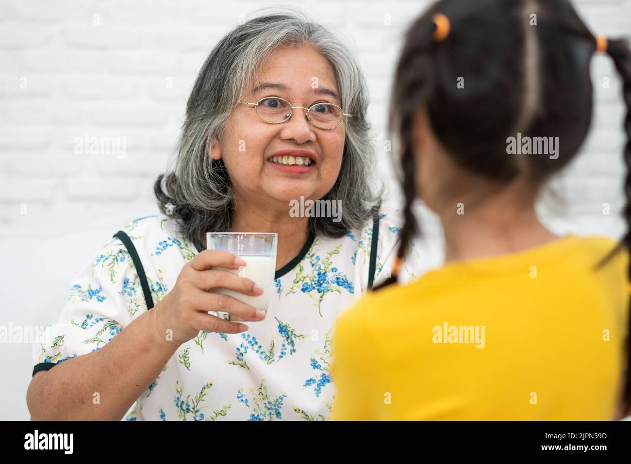 Happy elderly Asian Grandma sits beside her granddaughter and feeds ...
