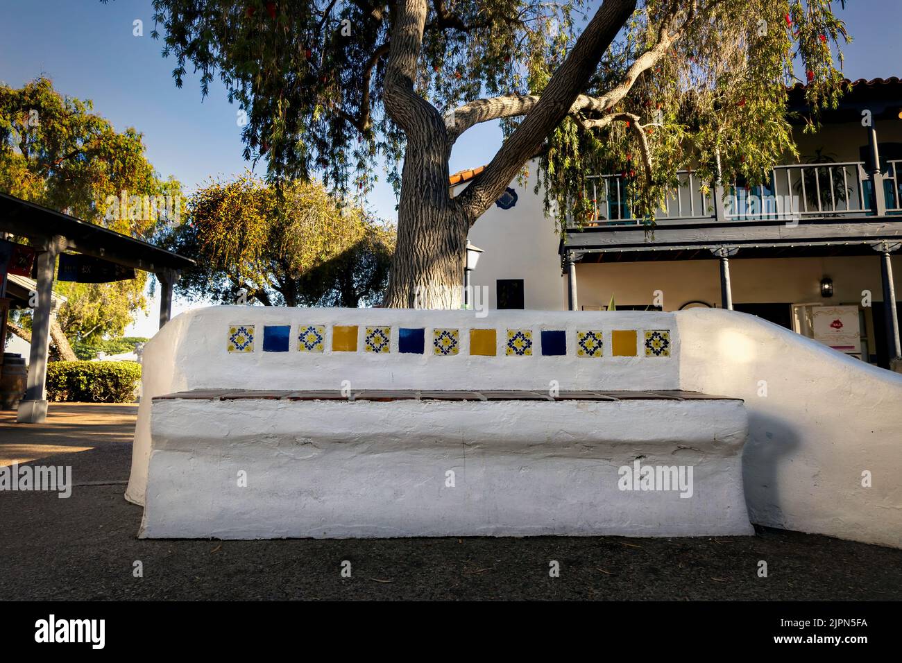 A simple white stone park bench, in a southwester style, sits under a ...