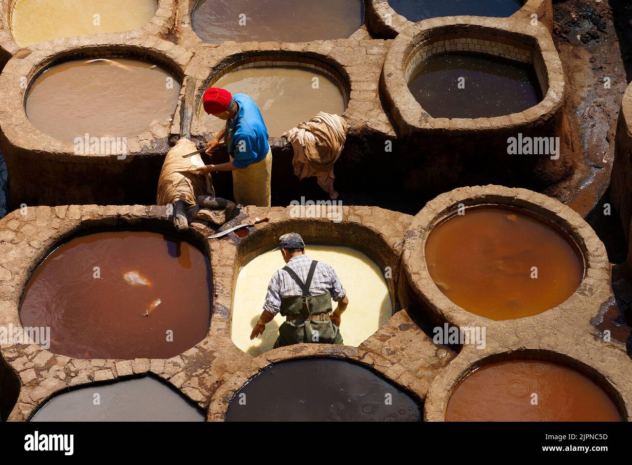 The round stone vessels with dye liquids and men working in famous ...