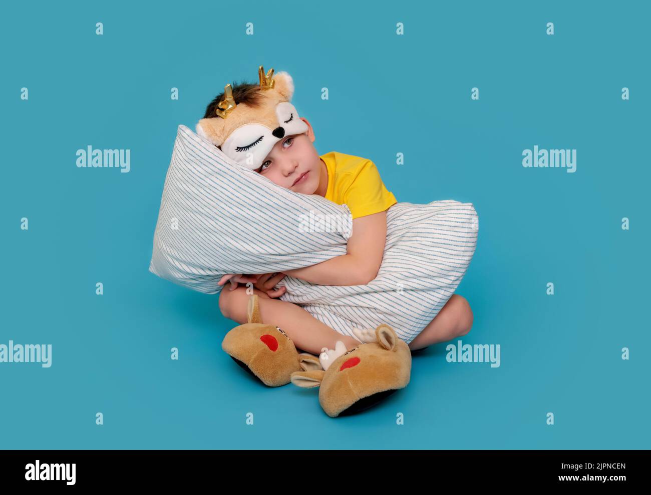 little boy with pillow, pajamas and sleep mask on a blue background ...