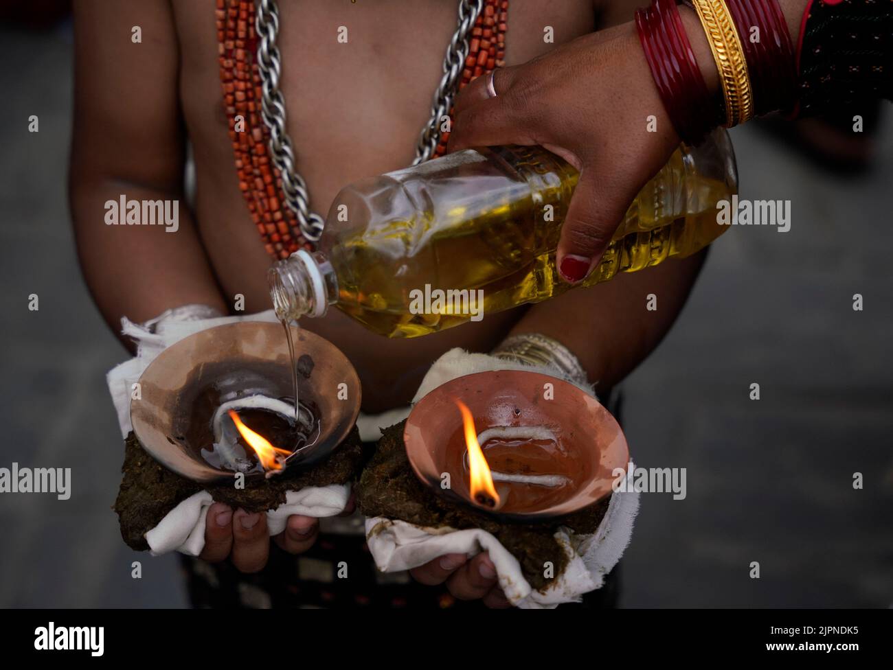 A devotee holds oil lamps that are being refilled while taking part in ...