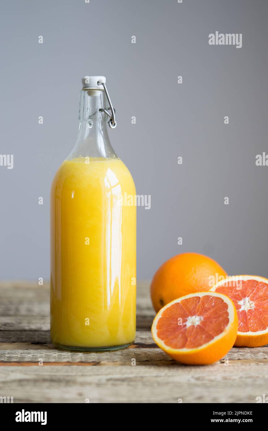 Glass bottle with orange juice and oranges on a wooden background. An ...