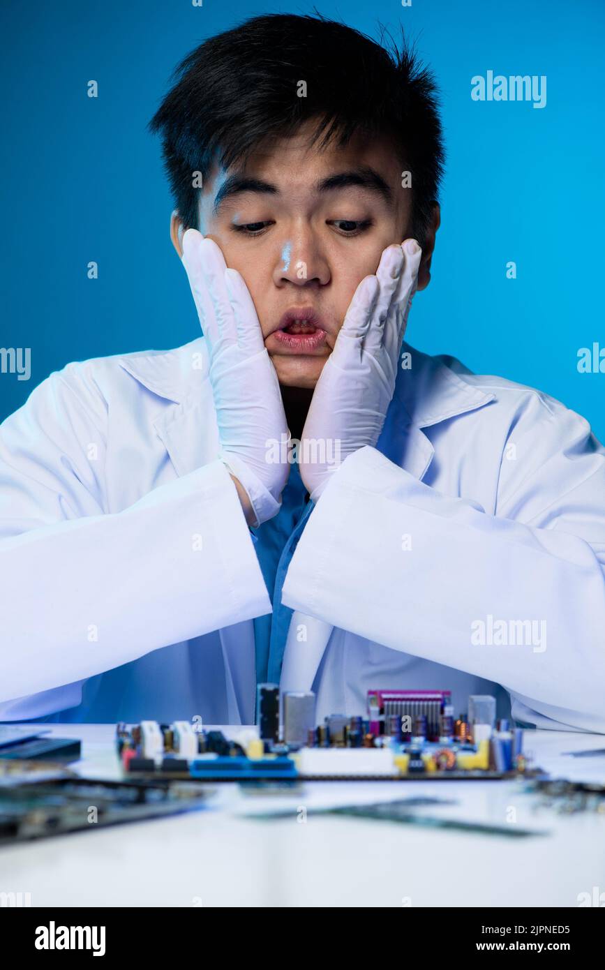 Frustrated Asian repairman looking at broken motherboard on his table ...