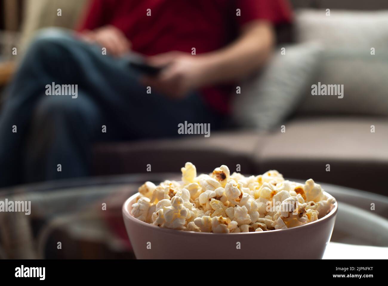 Caucasian man sitting on sofa with popcorn and tv remote Stock Photo ...