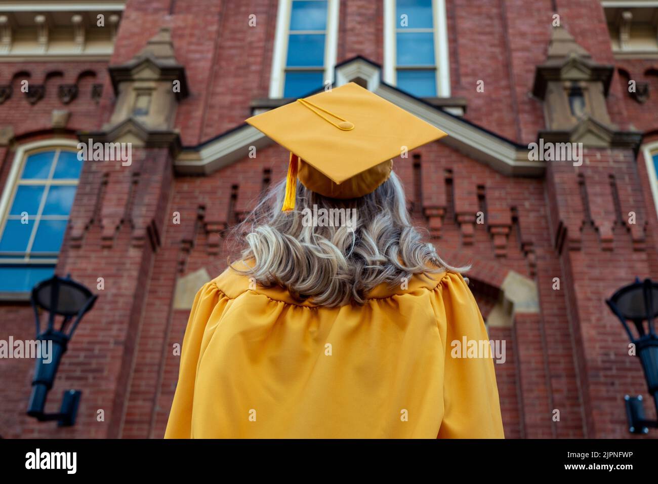 A girl in a yellow graduation robe standing against a red stone ...