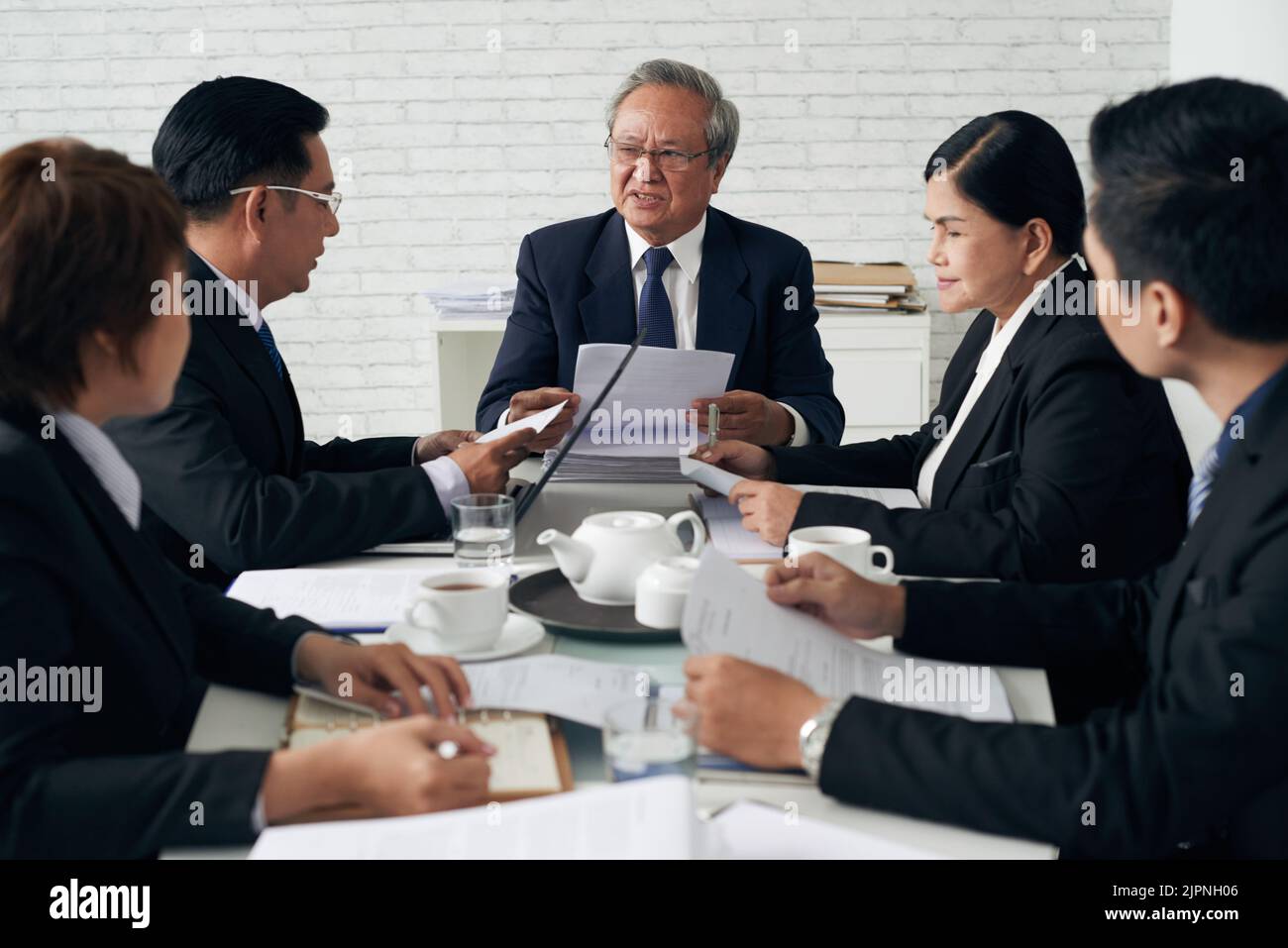 Unhappy senior Vietnamese lawyer discussing documents with his team ...