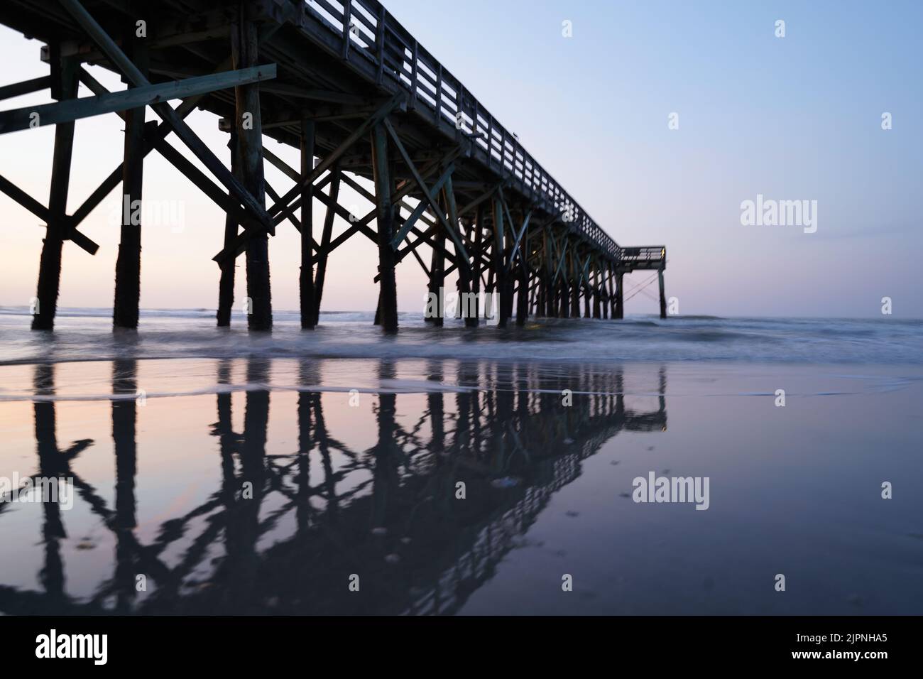 A pier symmetrically reflecting on the seawater at a beautiful sunset ...