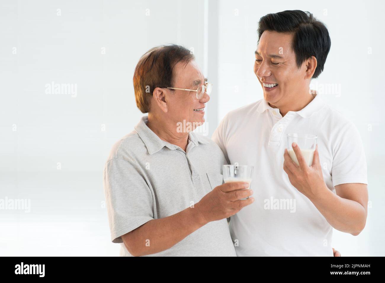 Happy Senior Asian Man Hugging His Adult Son And Drinking Milk Stock