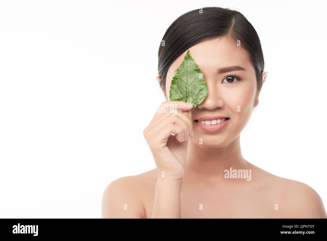 Smiling young Asian woman with flawless skin covering one eye with ...