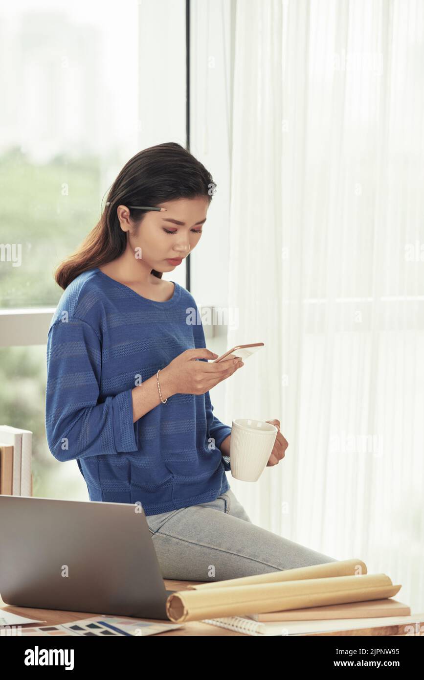 Architecture bureau manager drinking coffee and reading messages in her ...