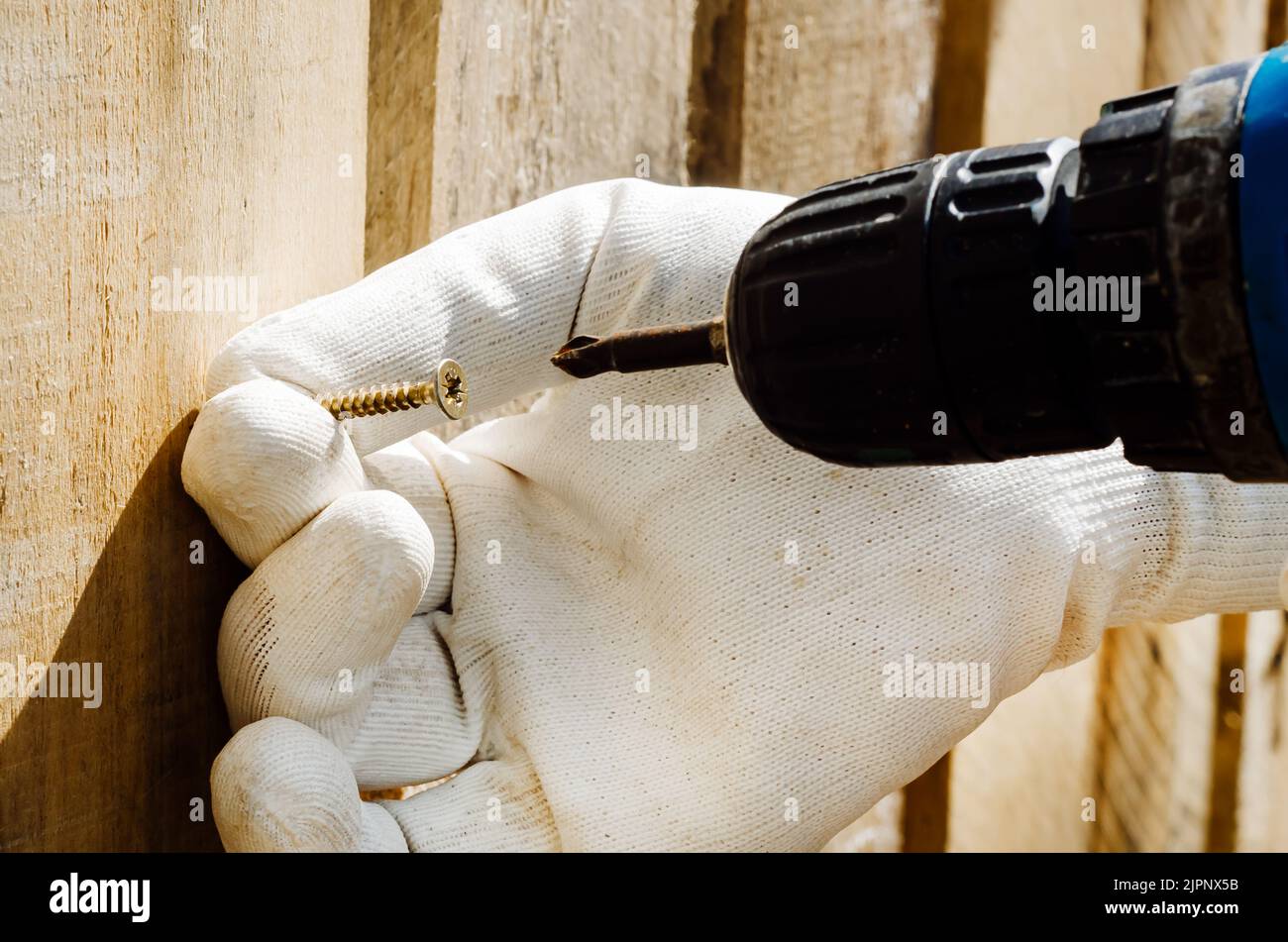 A hand with a screwdriver twists a screw into a wooden board ...