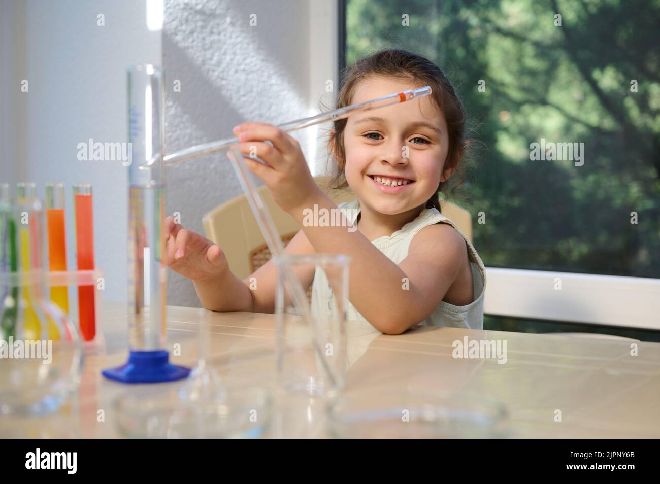 Charming little girl sitting at table with laboratory glassware ...