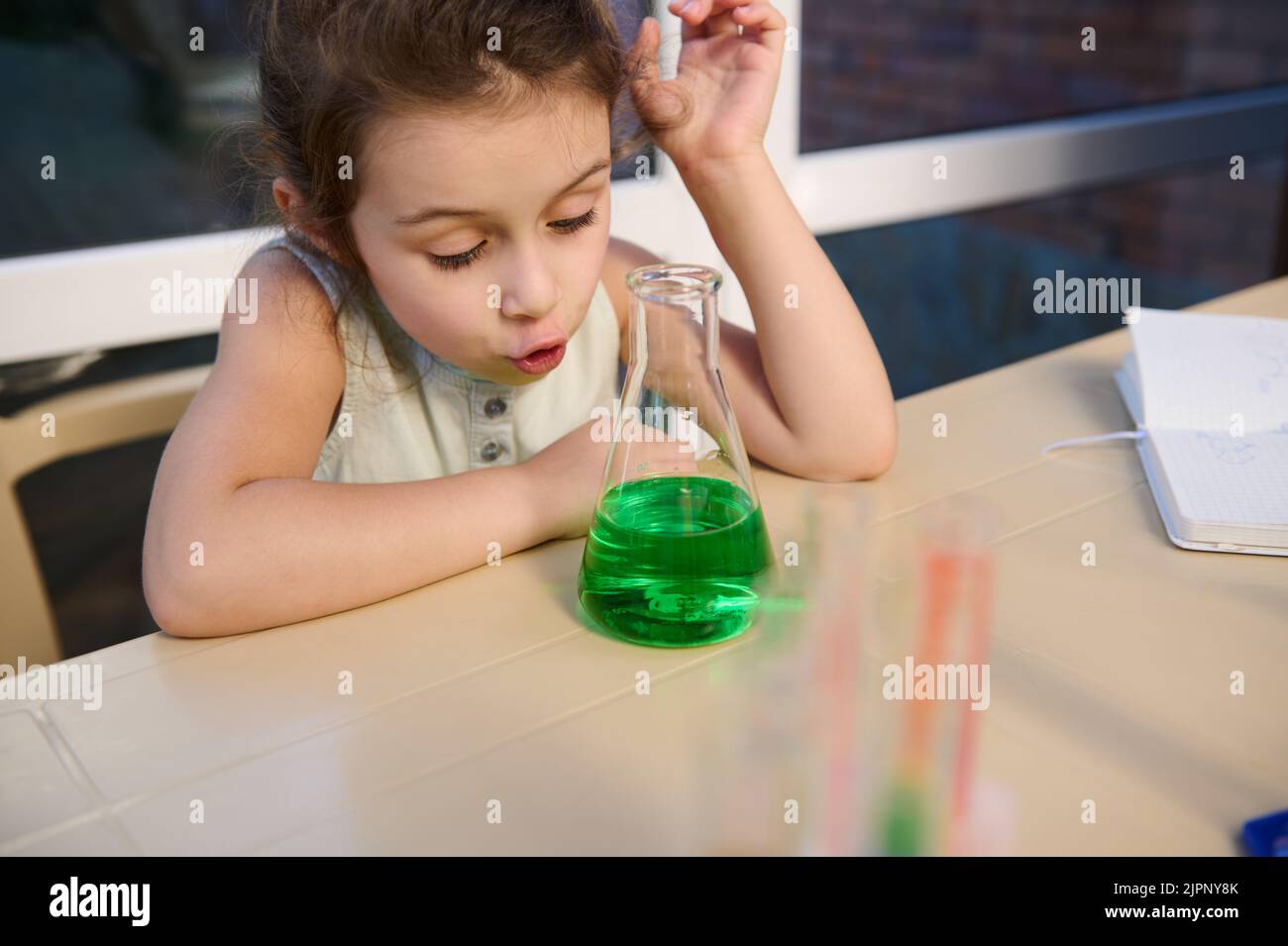 Adorable little school girl watching a chemical reaction in a flat ...