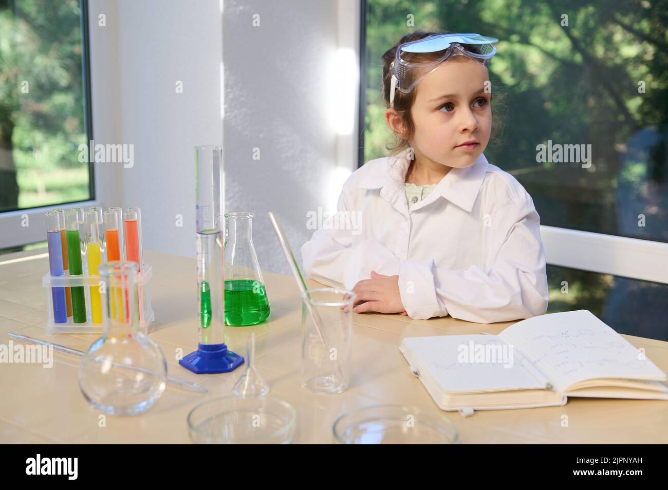 Adorable schoolgirl in protective eyeglasses and lab coat, enjoys ...