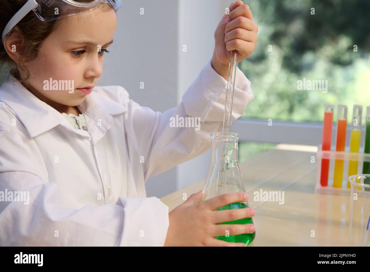 Little girl chemist using a pipette, dripping liquid chemicals into a ...