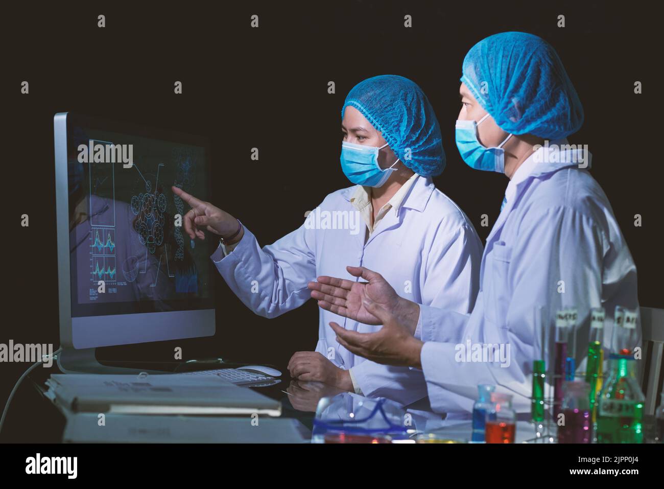 Group of talented Asian microbiologists wearing medical masks and white coats sitting in front ...