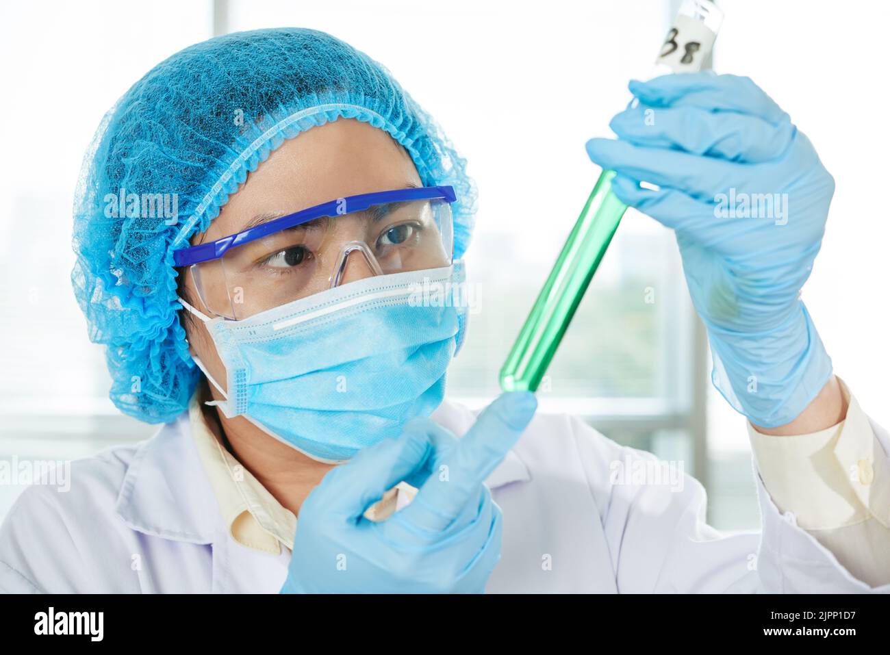 Pretty Asian researcher wearing white coat and medical mask studying ...