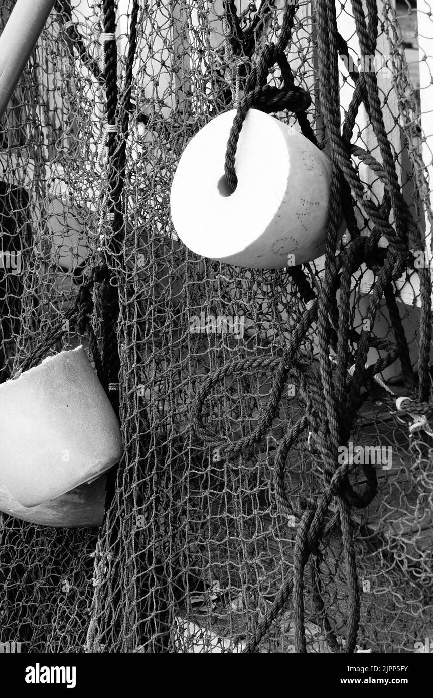 A grayscale shot of hanging fishing nets and floating round blue board ...