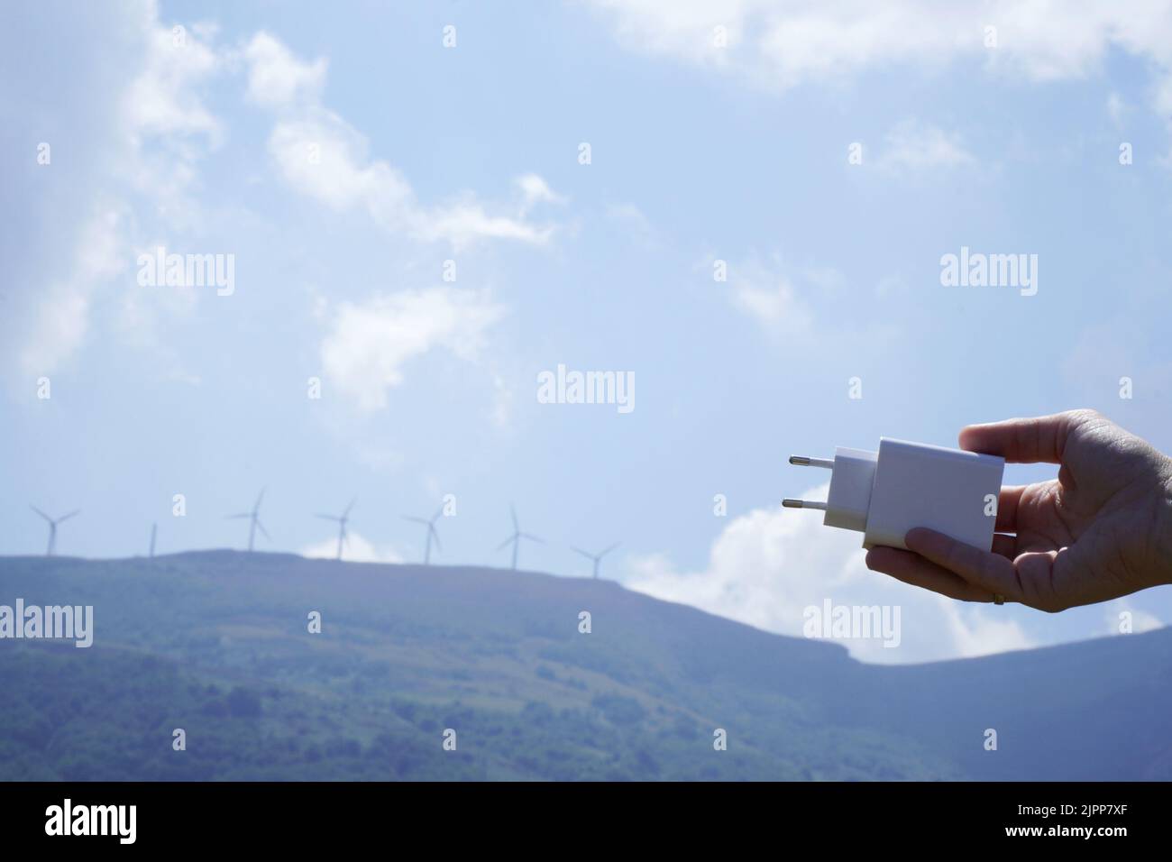 Wind power towers in the background with a hand holding a plug close up ...